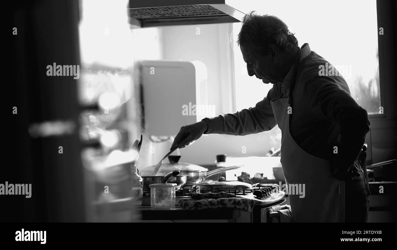 Monochrome scene of Elderly Chef Stirring Meal on Kitchen Stove, candid ...