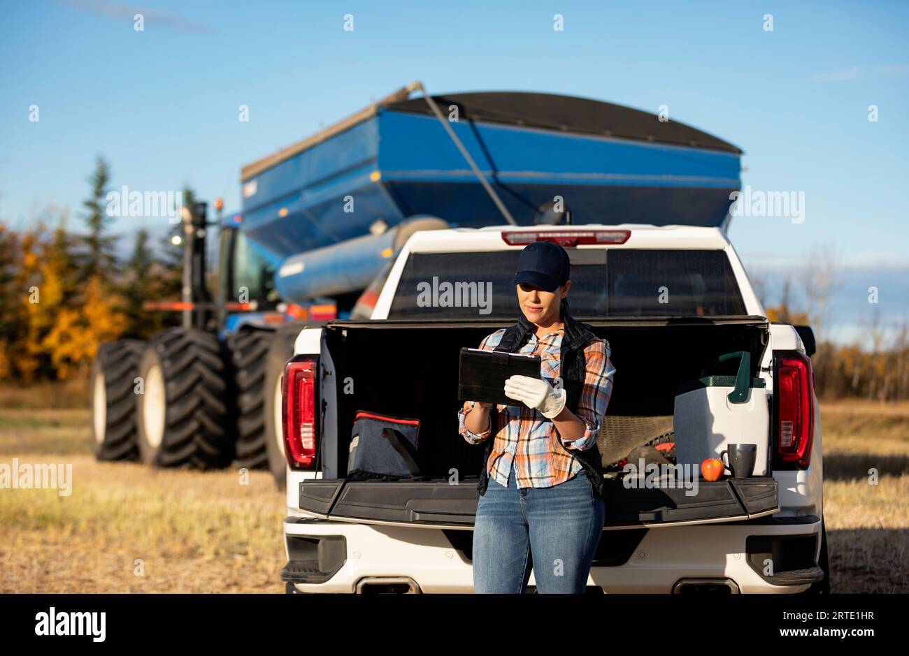A farmer leaning on the tailgate of a half-ton truck and using a ...