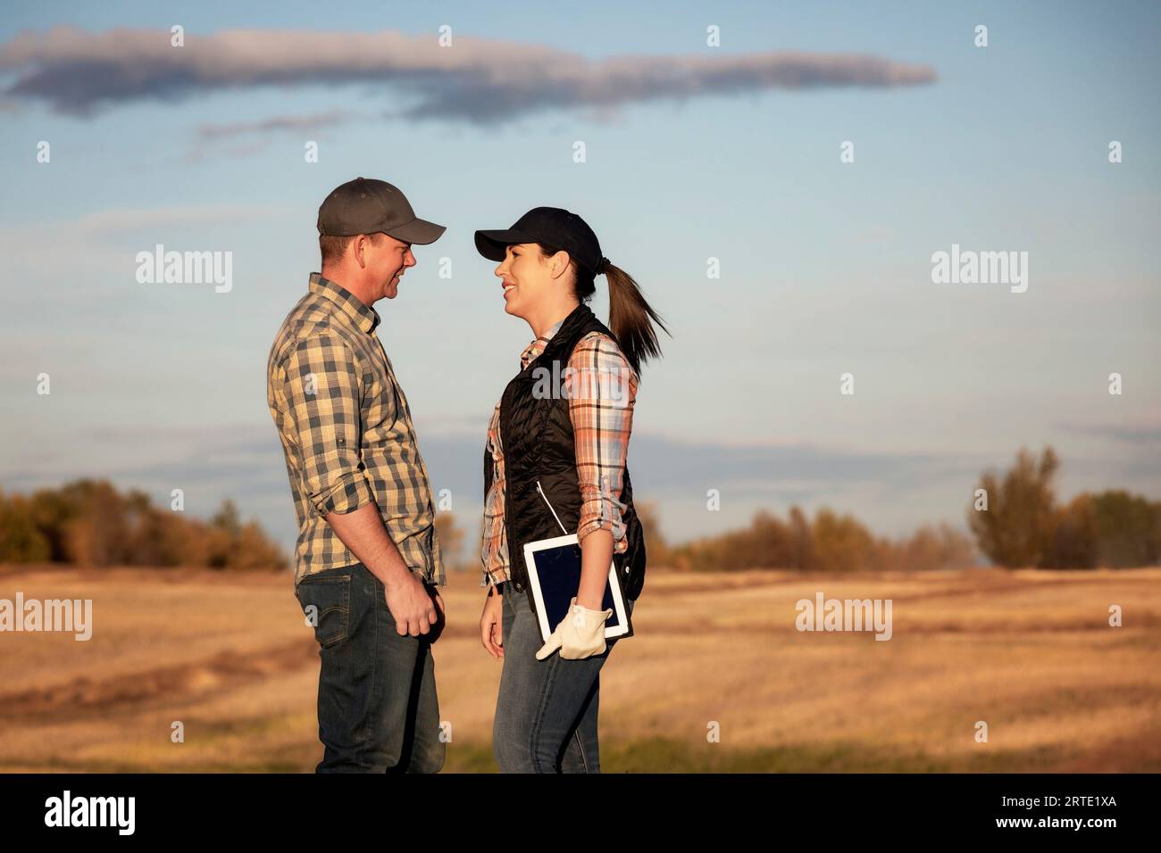 A farm couple using portable technologies, standing in a field face to ...