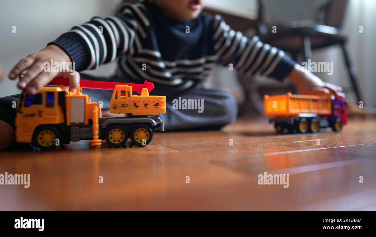 Small boy clashing trucks together seated on floor. Male child hitting ...