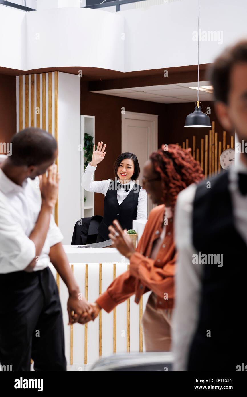 Couple saying goodbye to hotel employee, front desk staff waving at ...