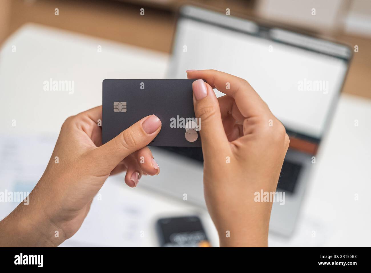 Female holds dark credit card for online payment at desk with documents ...
