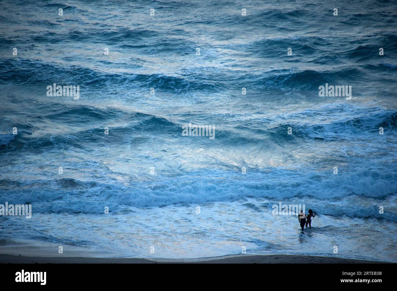 Couple plays in the ocean waves at dusk at Riviera Beach in Florida ...