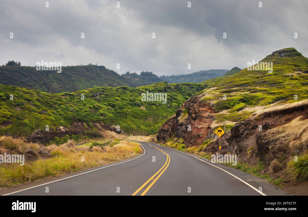 Winding road with traffic sign and cloudy sky through the green hills ...