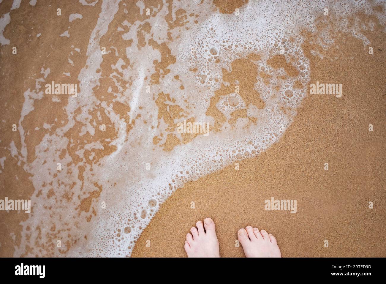 Viewpoint, looking down at feet standing next to foamy surf on Kamaole ...
