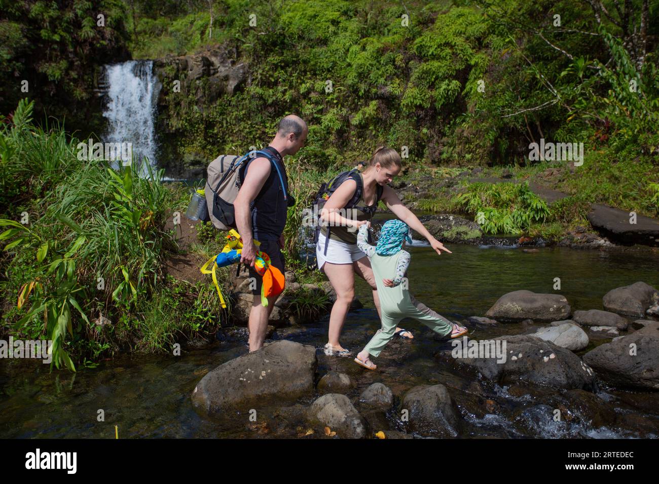 A family carefully walking on a path of volcanic rocks while crossing a ...