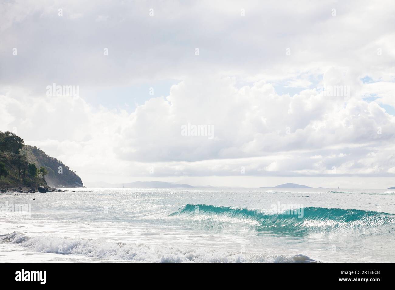 Turquoise wave and foamy surf rolling onto the shore against a pale ...