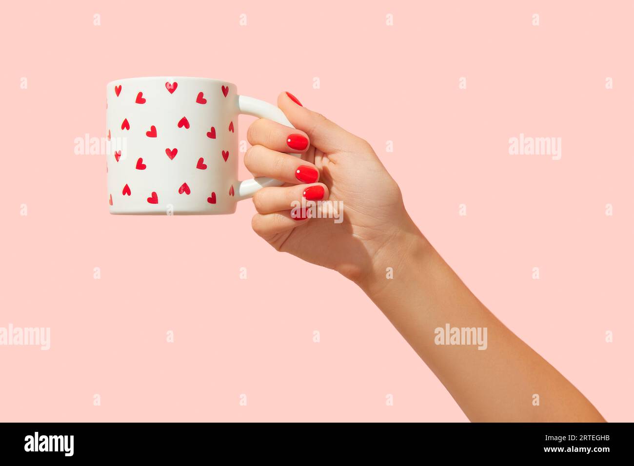 Womans hand with red manicure holding cup on pink background ...