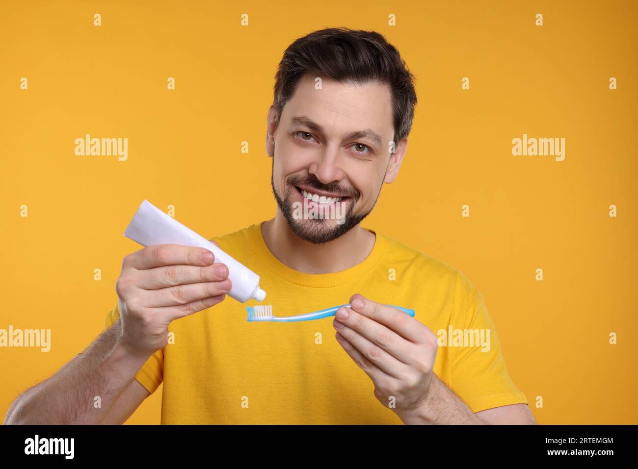 Happy man squeezing toothpaste from tube onto plastic toothbrush on ...