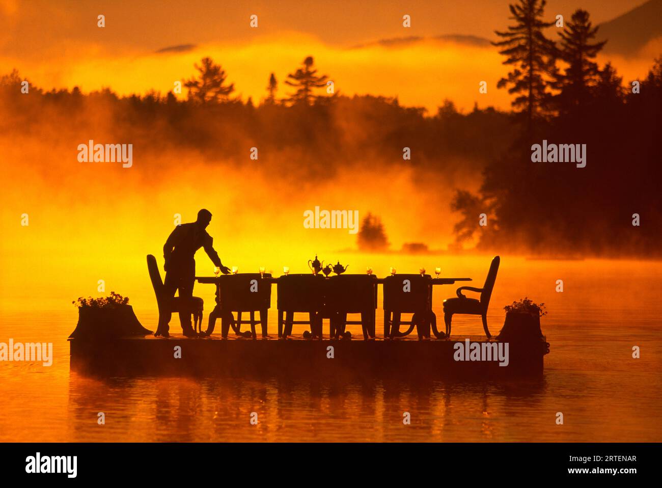 Silhouetted waiter setting a table on floating dining room at sunrise ...