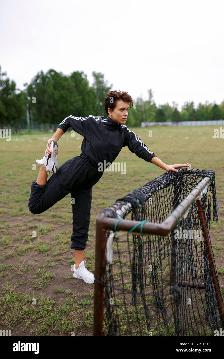 Young woman stretching legs while leaning on mini soccer goal Stock ...