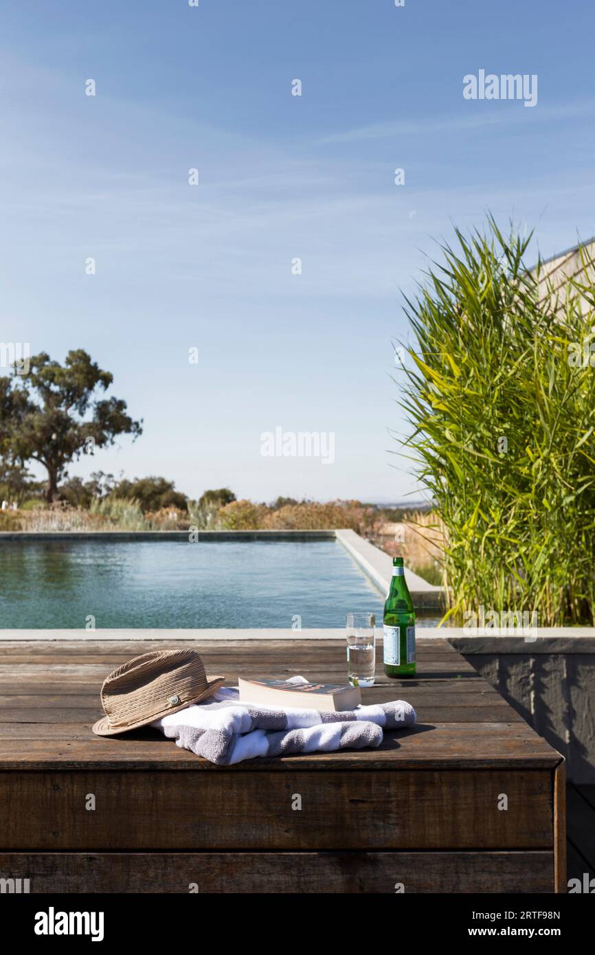 Inviting modern poolside retreat with a wooden bench, hat, sunglasses ...