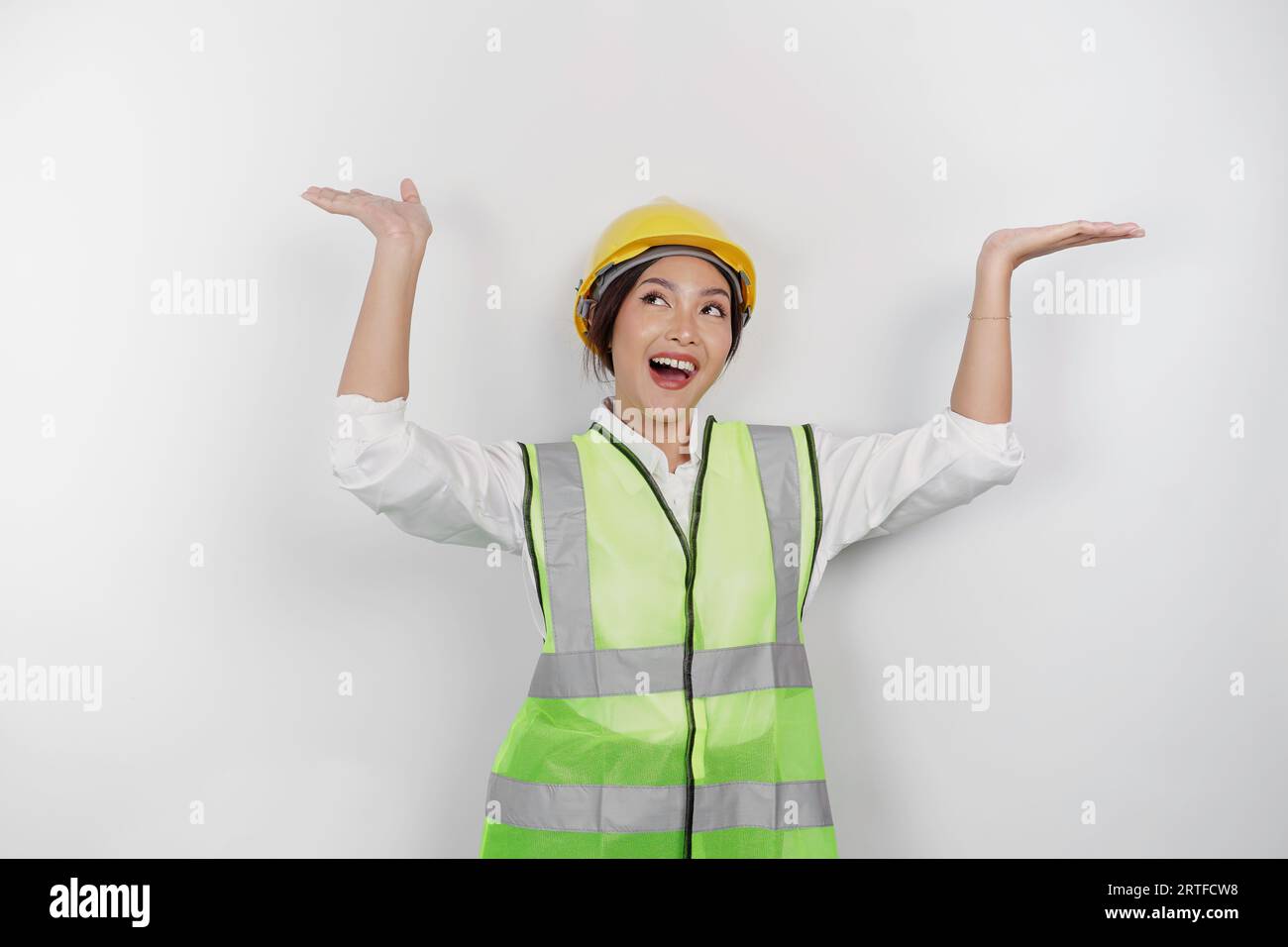 A smiling Asian woman labor wearing safety helmet and vest, pointing to ...