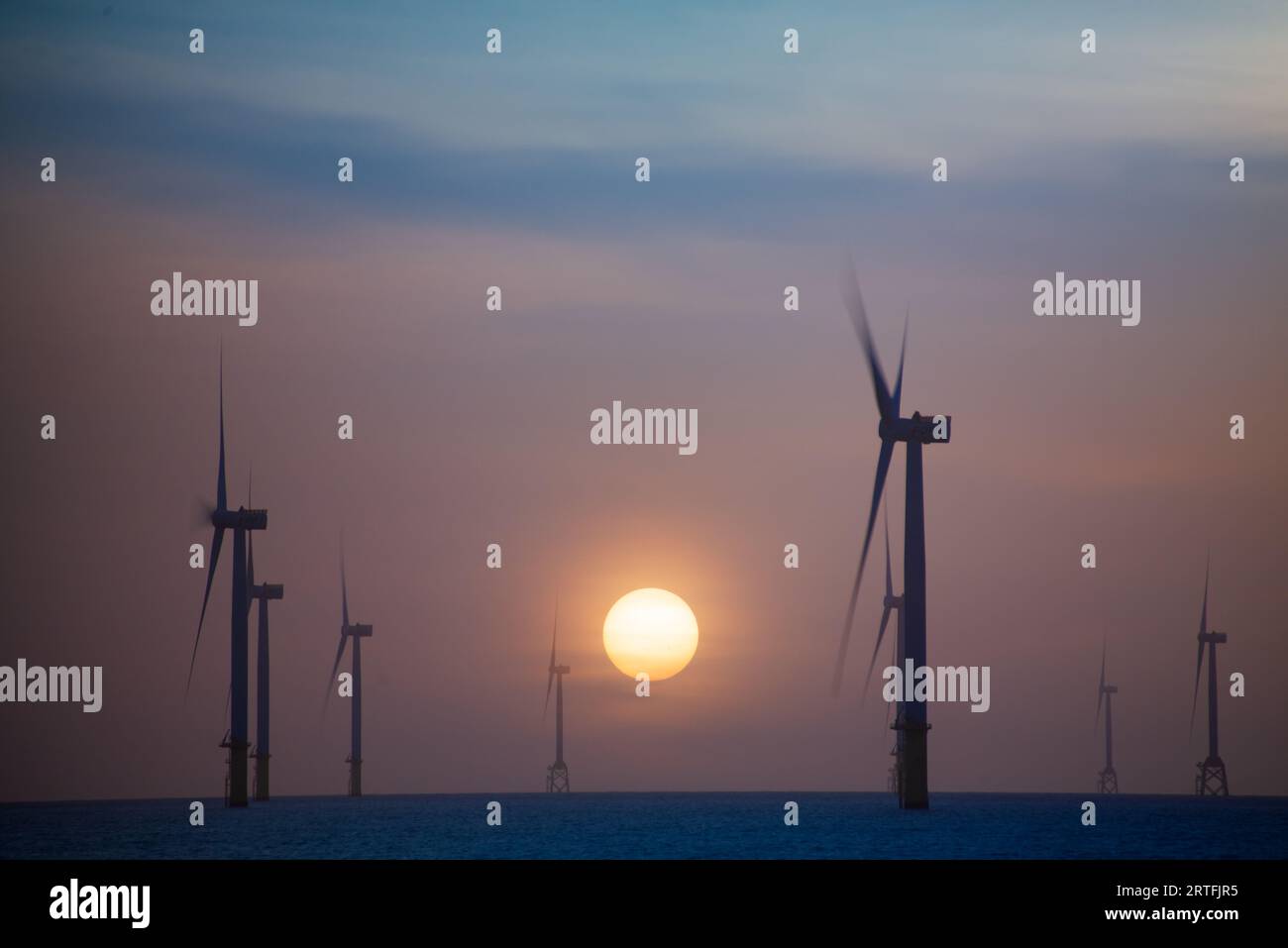 Fans of wind turbines spin over the sparkling sea. Dynamic clouds at ...