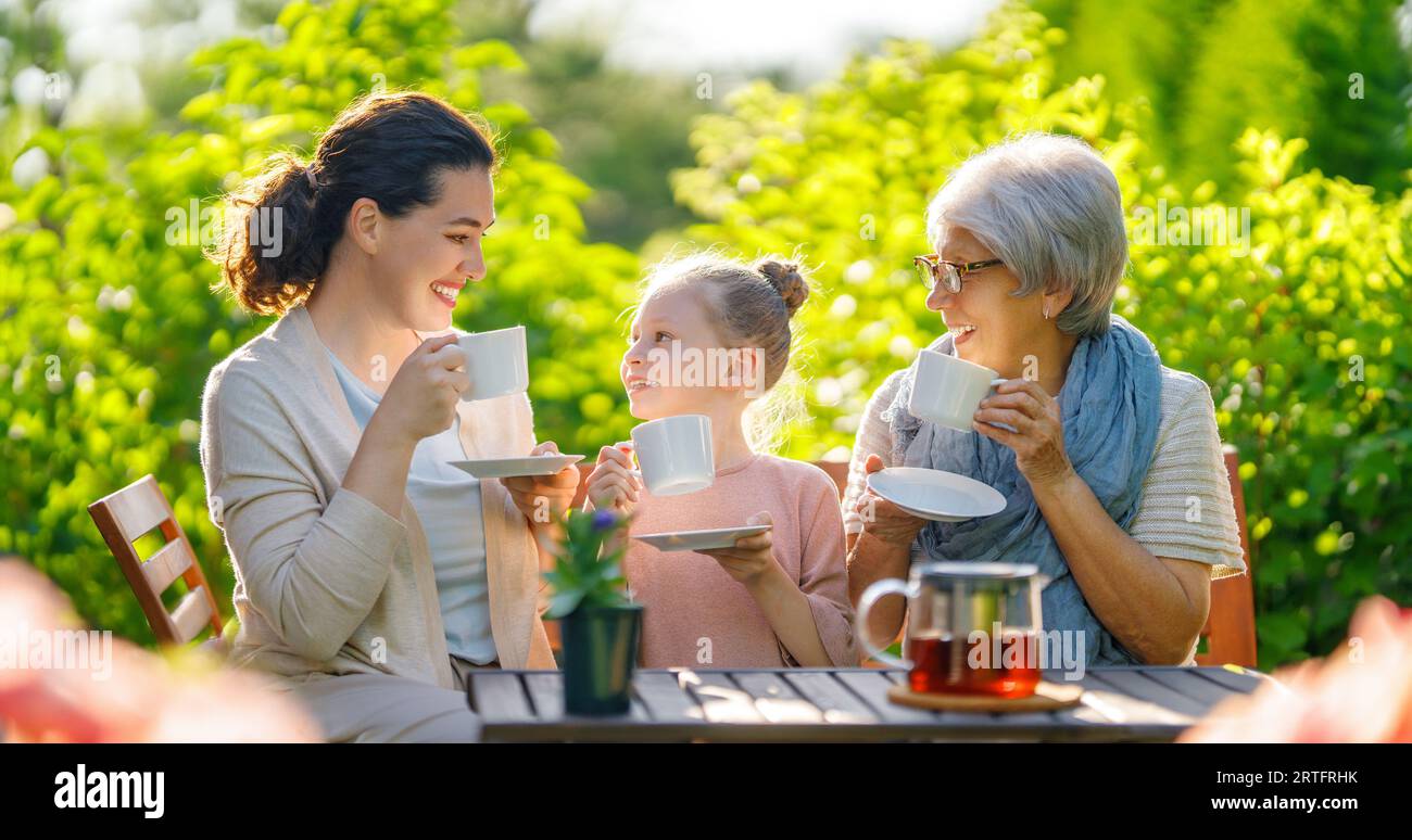 Happy little girl, her mother and grandmother drinking tea in summer ...