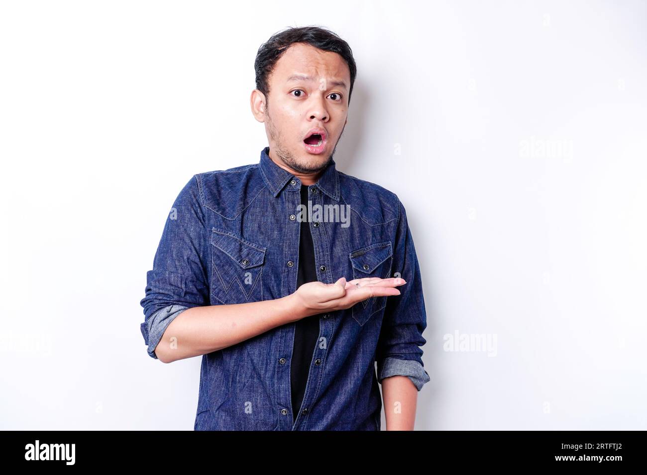 Shocked Asian man wearing blue shirt pointing at the copy space beside ...