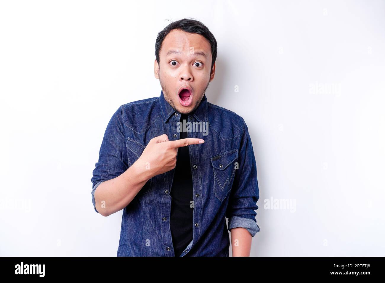 Shocked Asian man wearing blue shirt pointing at the copy space beside ...