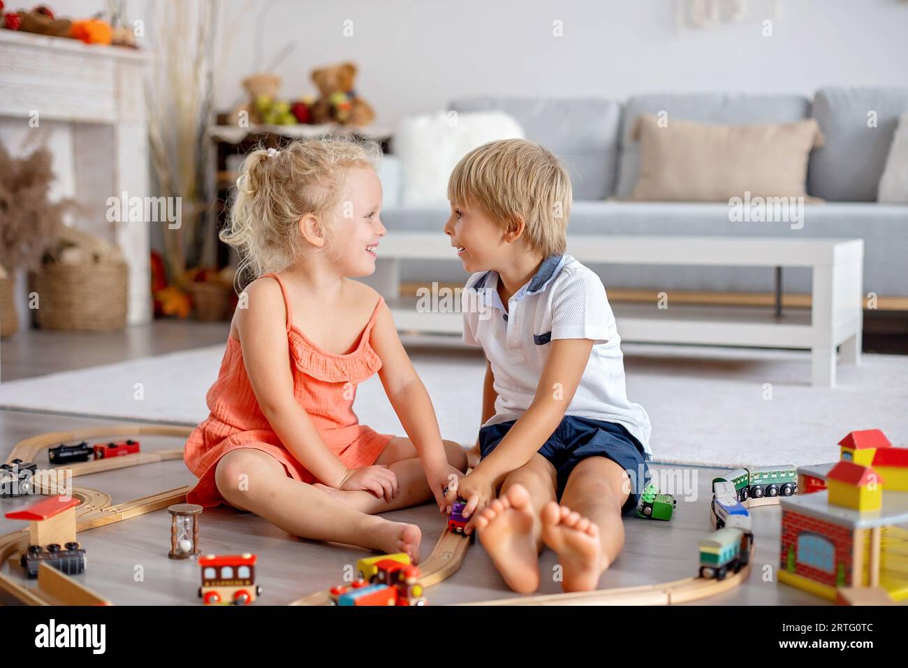 Two sweet children, siblings, playing with trains at home together ...