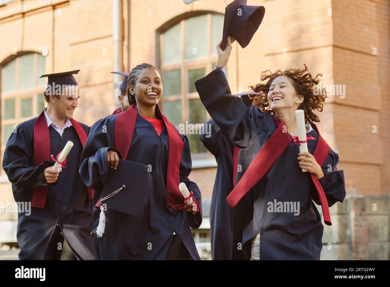 Happy graduated students in robes running along the campus outdoors ...