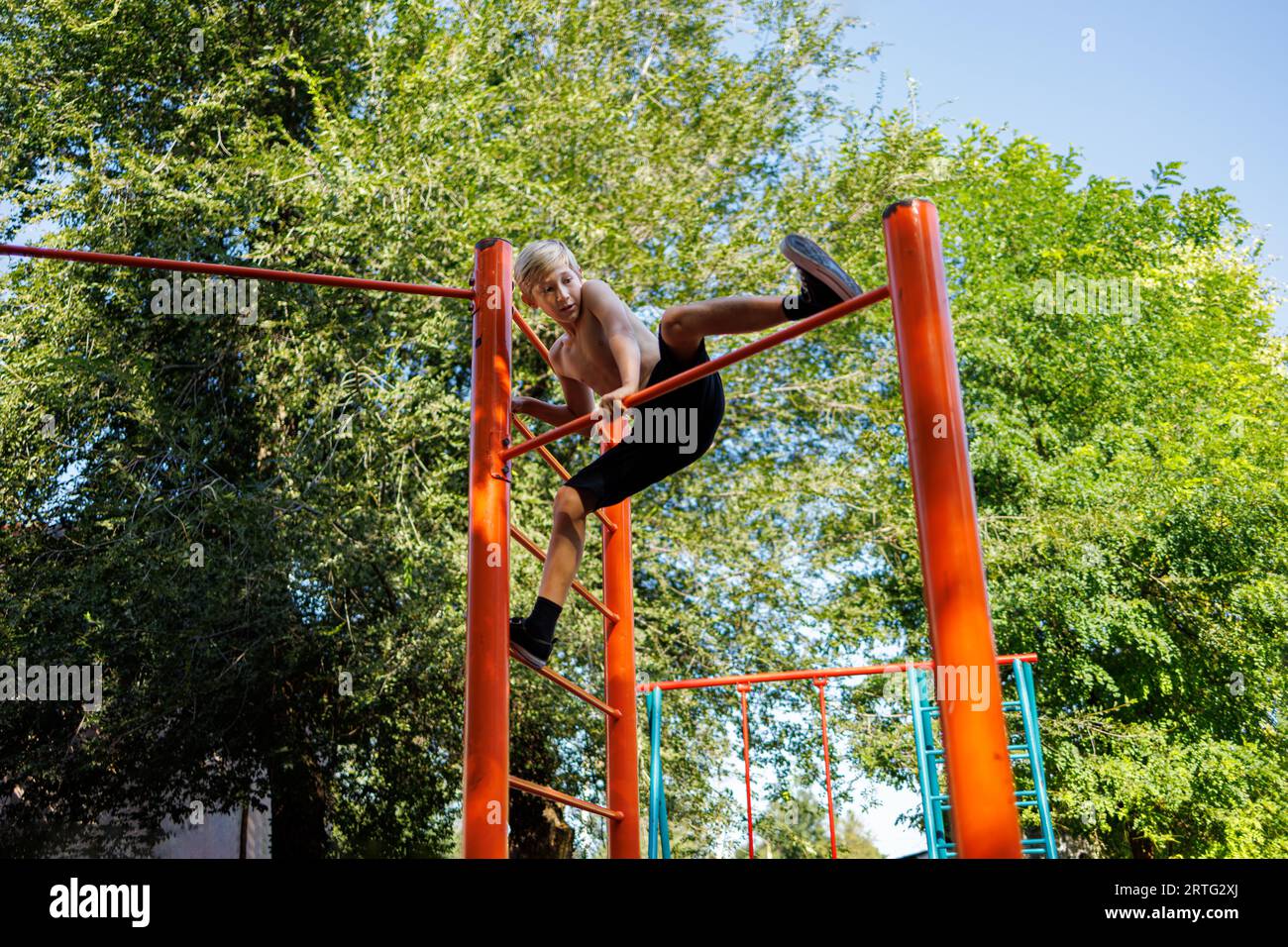 A boy athlete climbs the crossbar to perform a formal element. Street ...