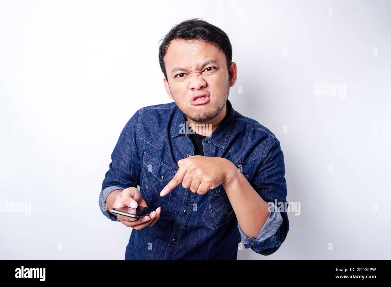 The angry and mad face of Asian man in blue shirt holding his phone ...