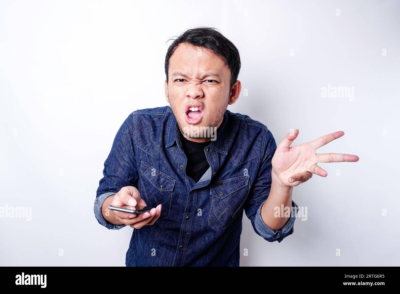 The angry and mad face of Asian man in blue shirt holding his phone ...
