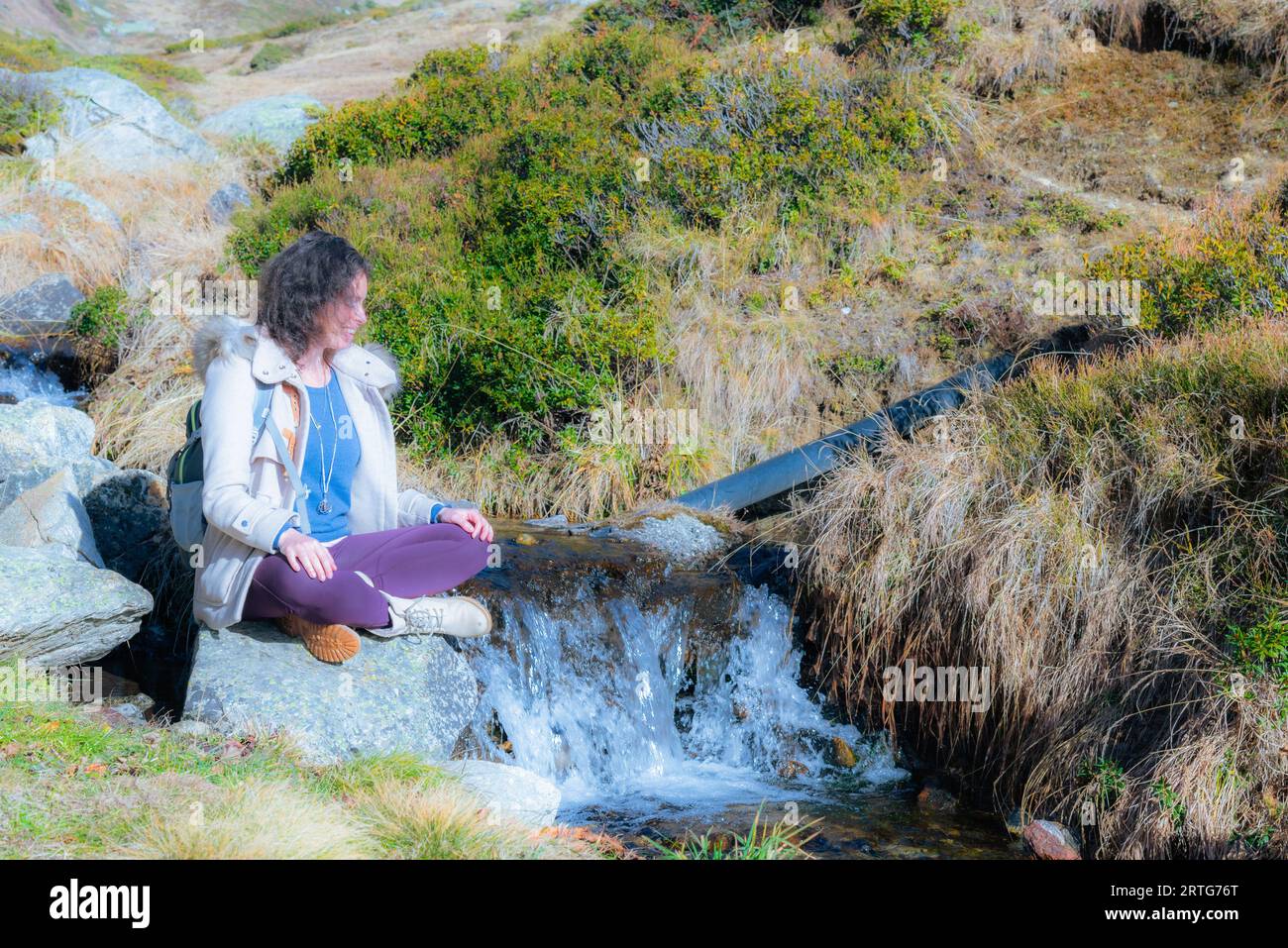 Relaxed traveler woman sitting on a rock next to a water stream in the ...