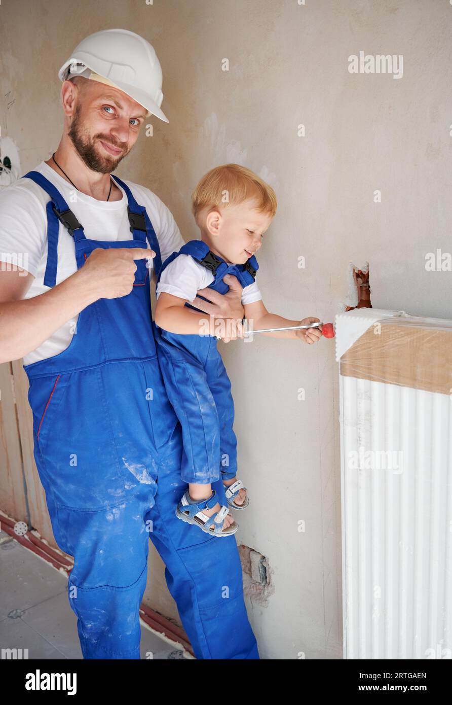Man plumber in work overalls pointing at baby boy and smiling while ...