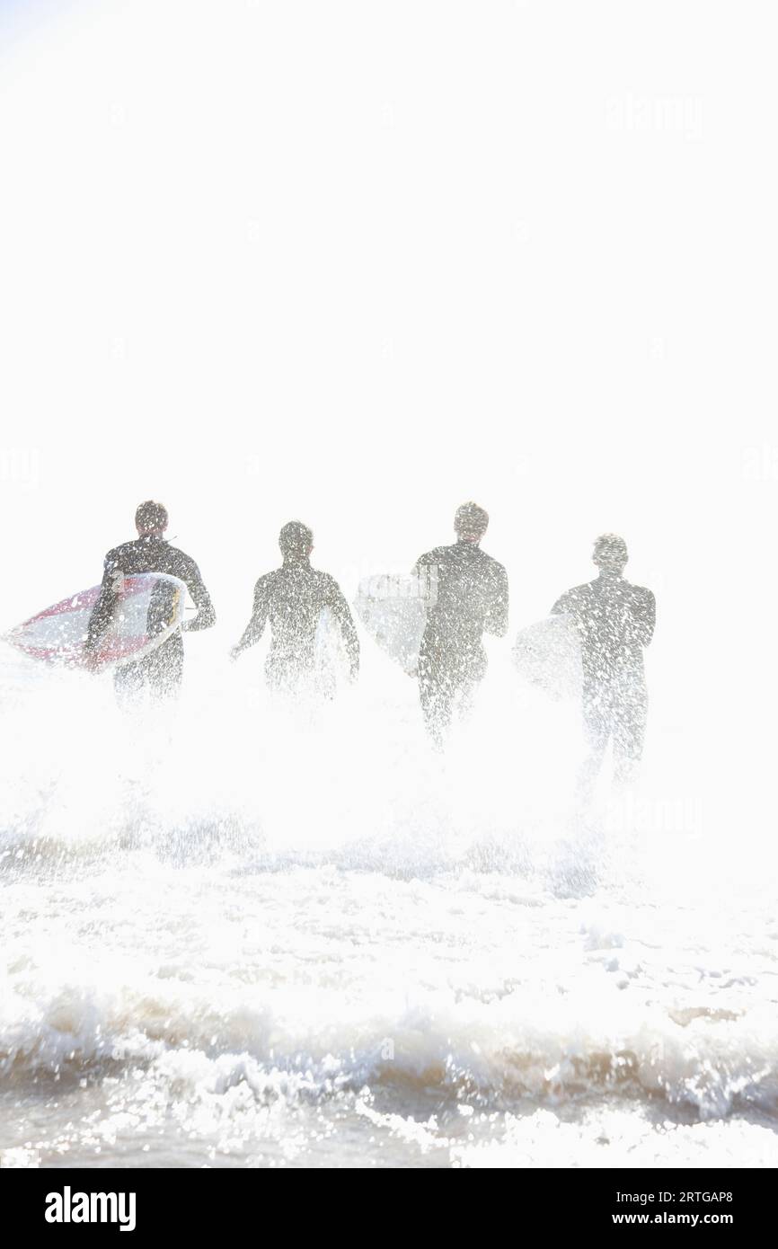 Back view of surfers running in the sea holding surfboards Stock Photo ...
