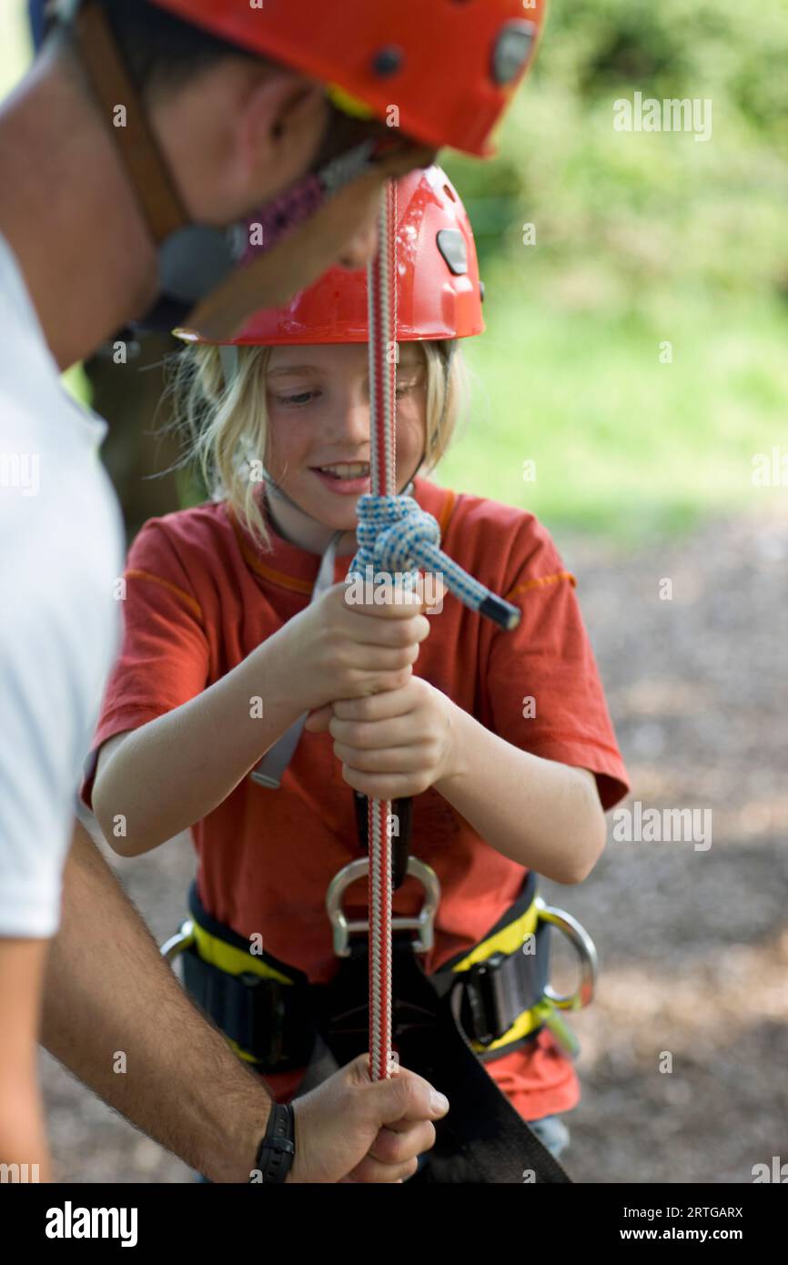 Young boy holding onto climbing rope with man helping her Stock Photo ...