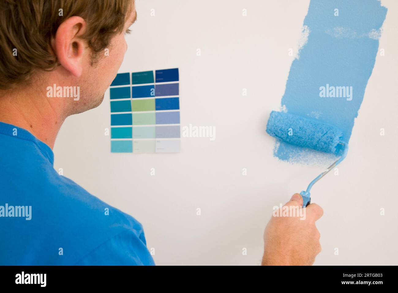 Back view of man holding paint roller and painting a white wall with ...