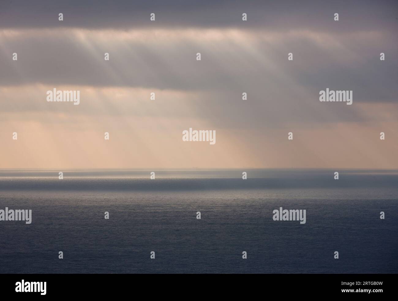 Grey sky with rain and sun rays shining on the ocean Stock Photo - Alamy
