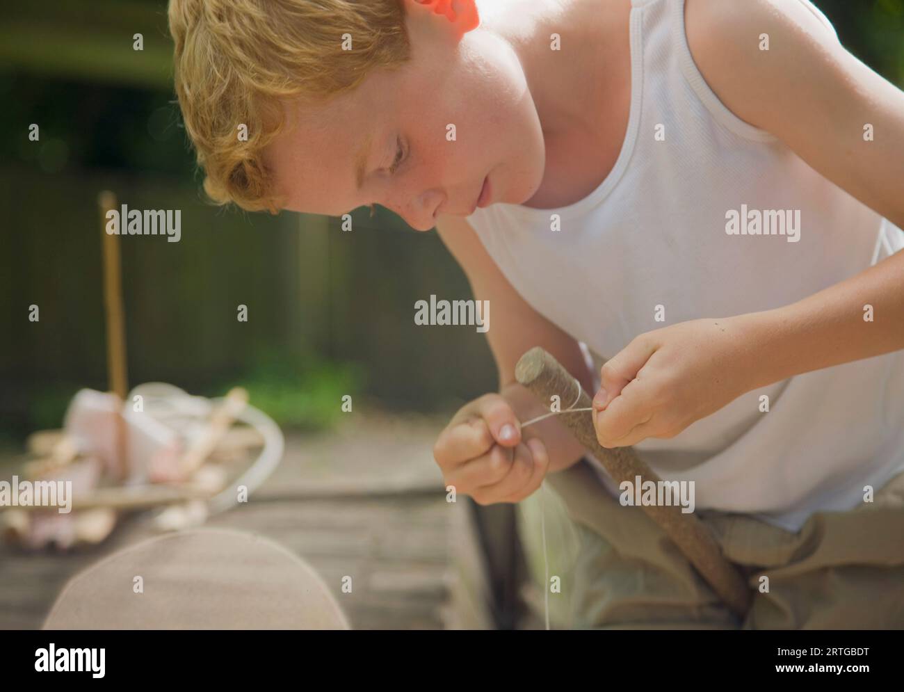 Young boy tying a knot with a string around a wooden stick Stock Photo ...