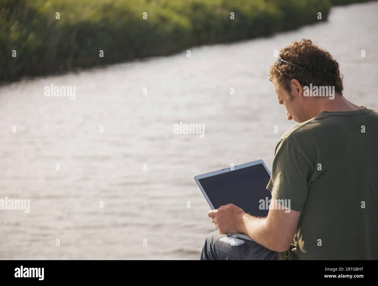 Back view of a man sitting by a river using a laptop computer Stock ...