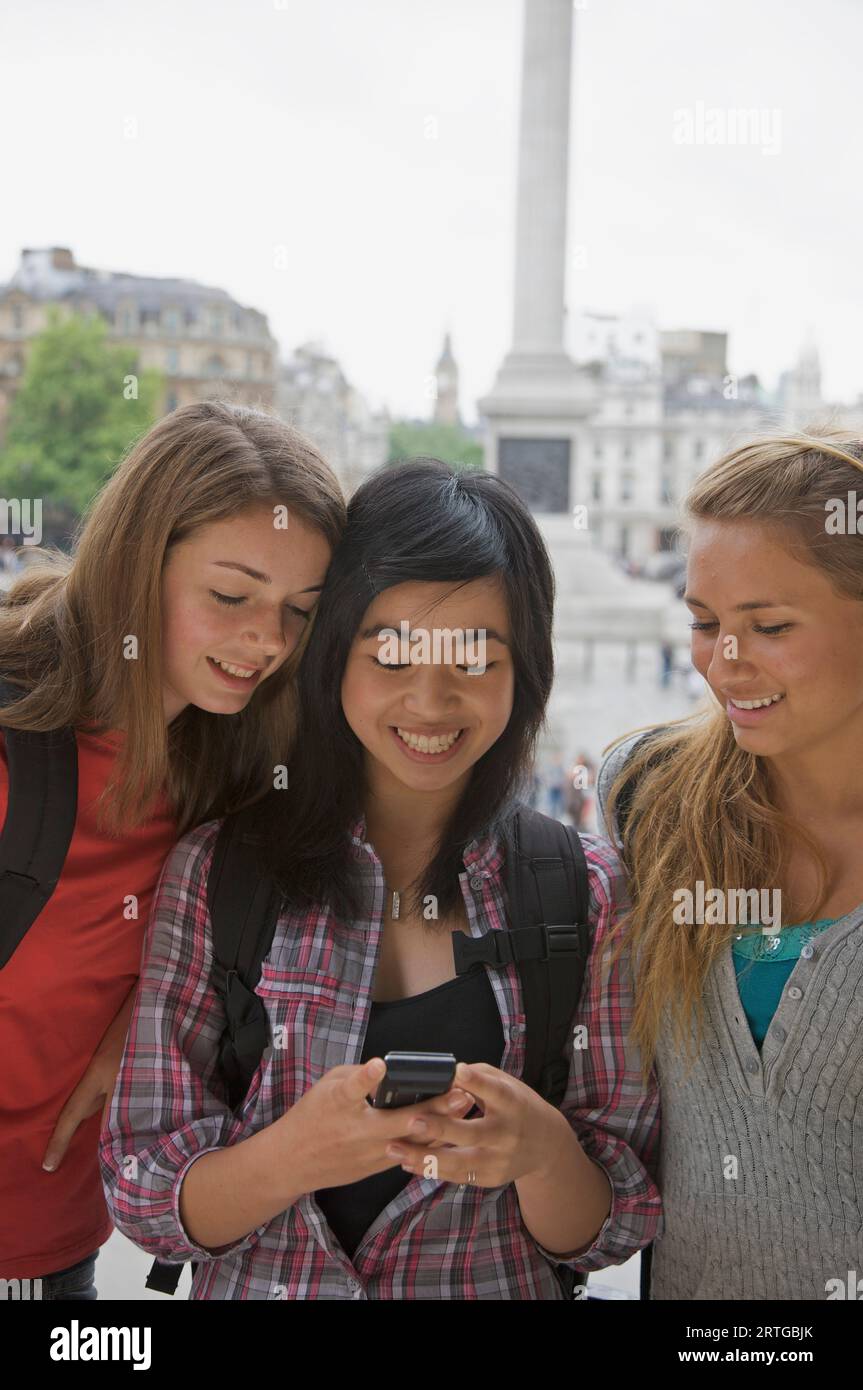 Three smiling teenaged girls using a cell phone in London Trafalgar ...