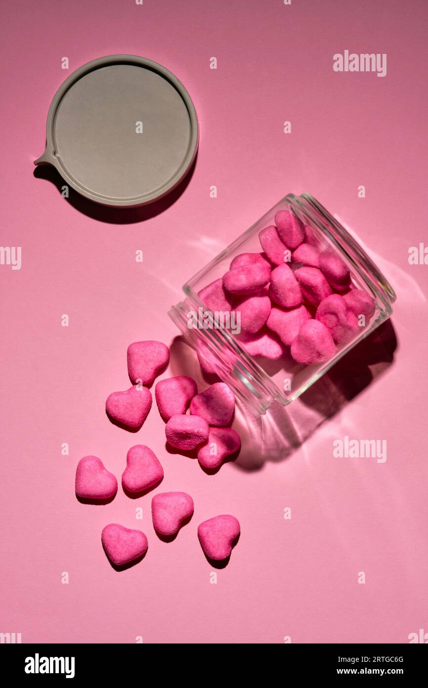 Pink candy hearts spilling from glass jar on pink background Stock ...