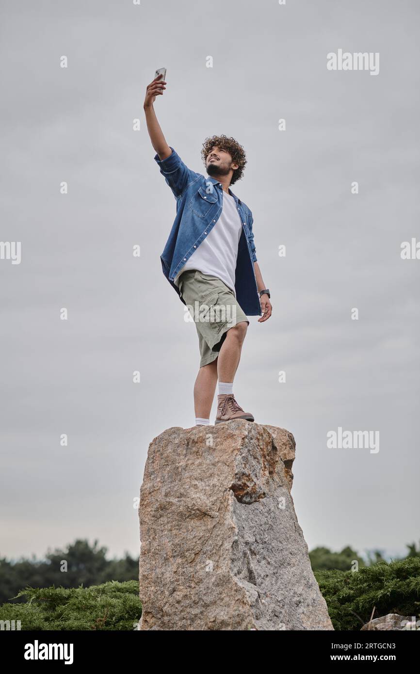 nomadism concept, curly indian man standing on rock and holding ...
