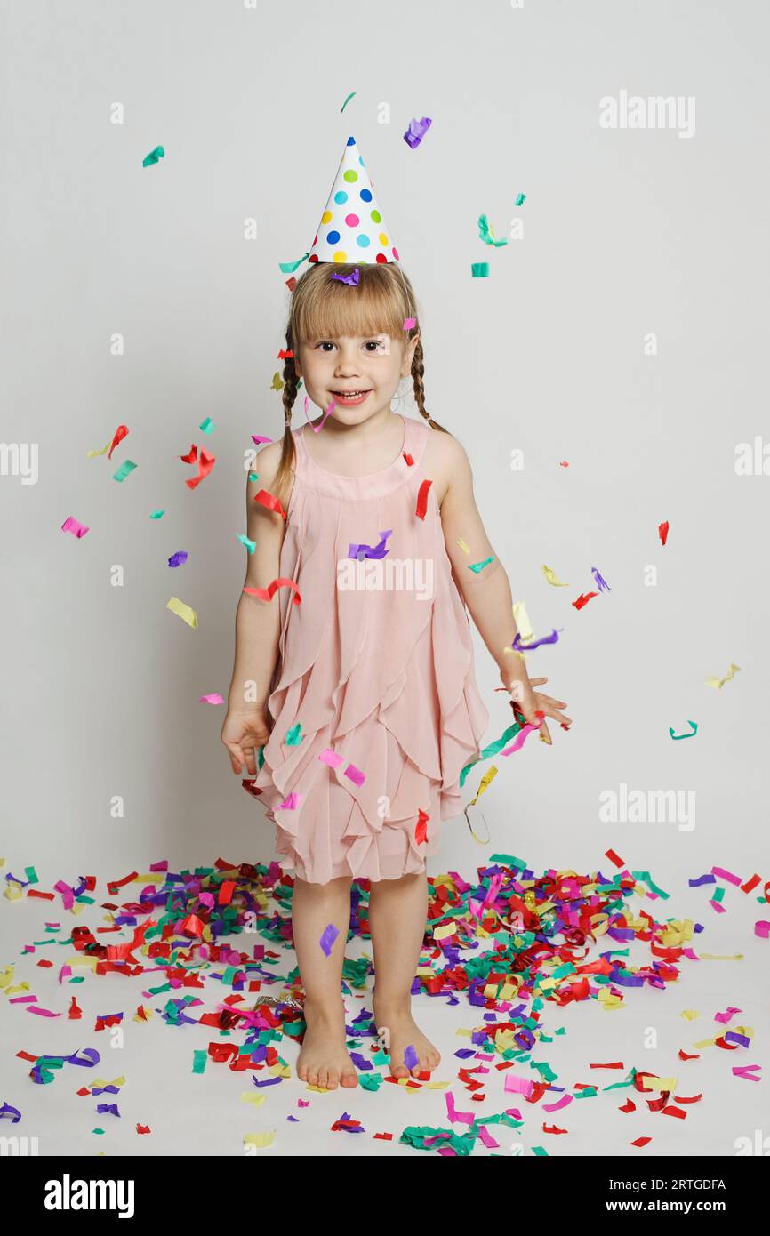 Happy kid girl standing with confetti against white studio wall ...