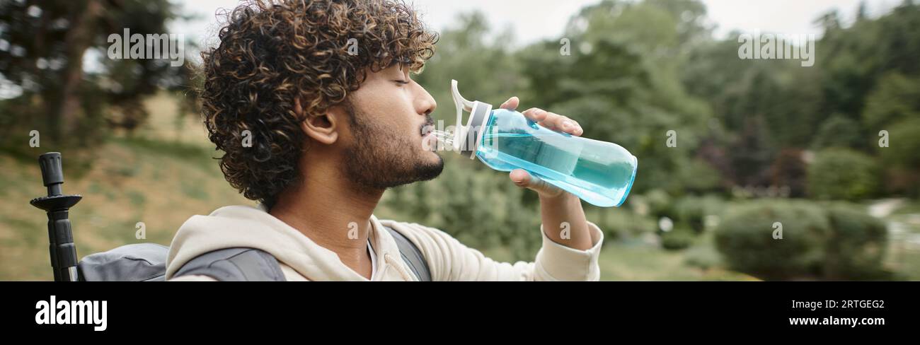 side view of indian backpacker drinking water with landscape on ...