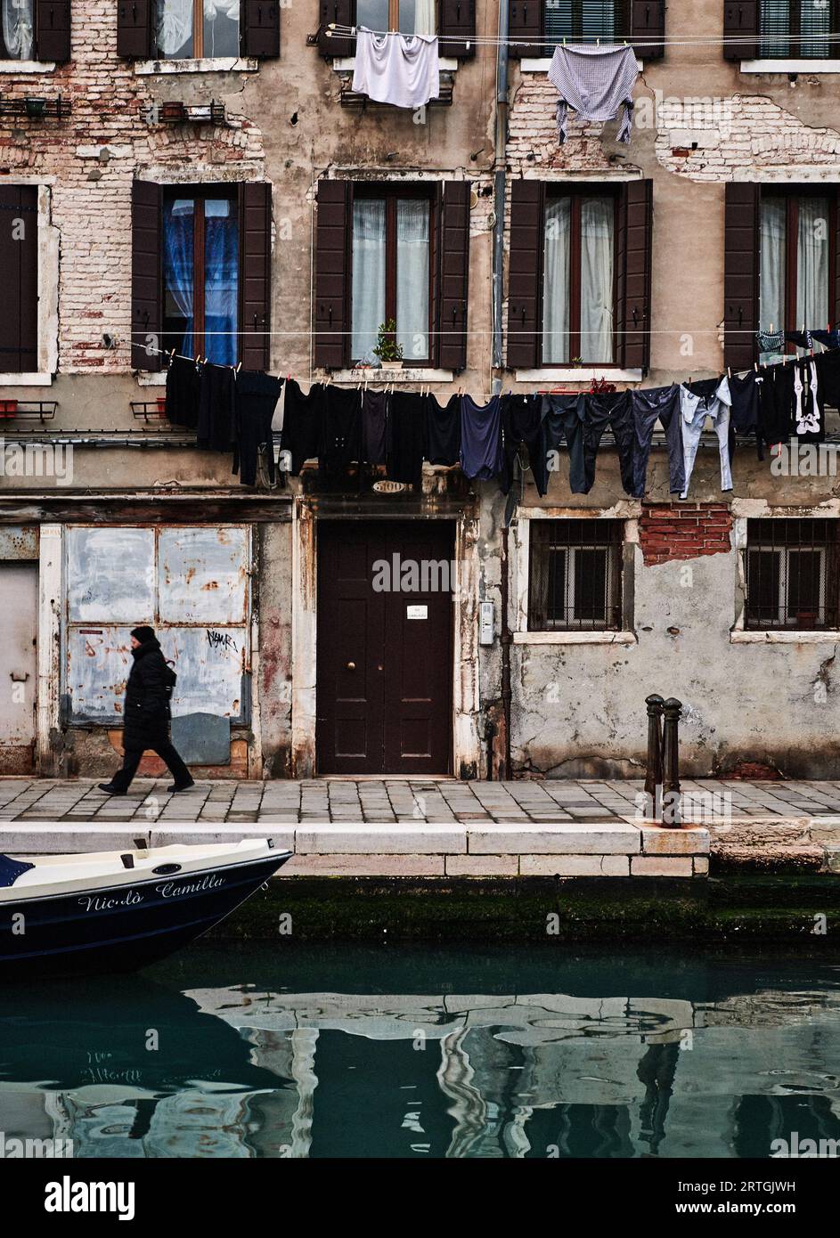 man in black walking along Venetian canal, old historic townhouse ...