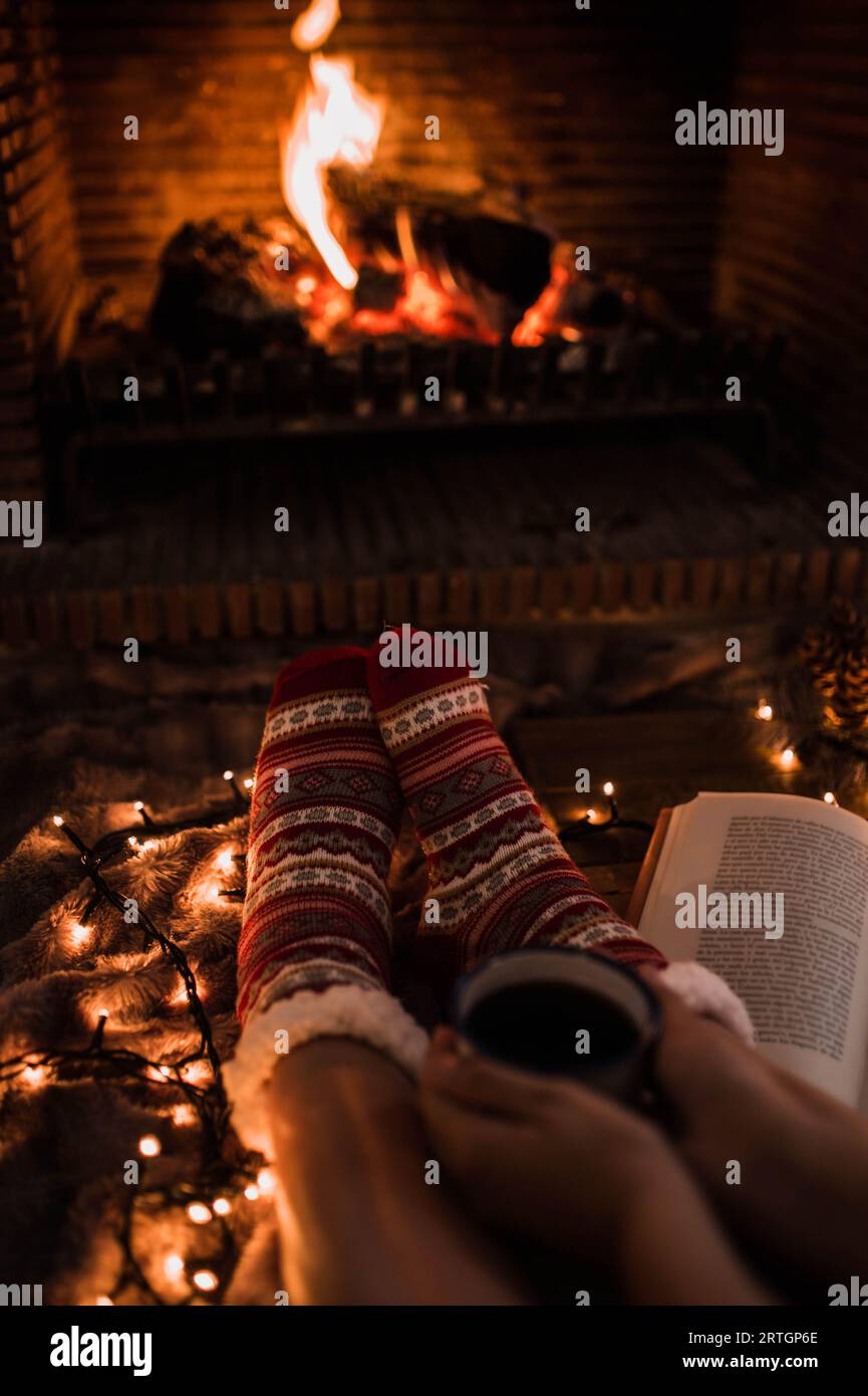 Faceless woman sitting by fireplace and holding mug Stock Photo - Alamy