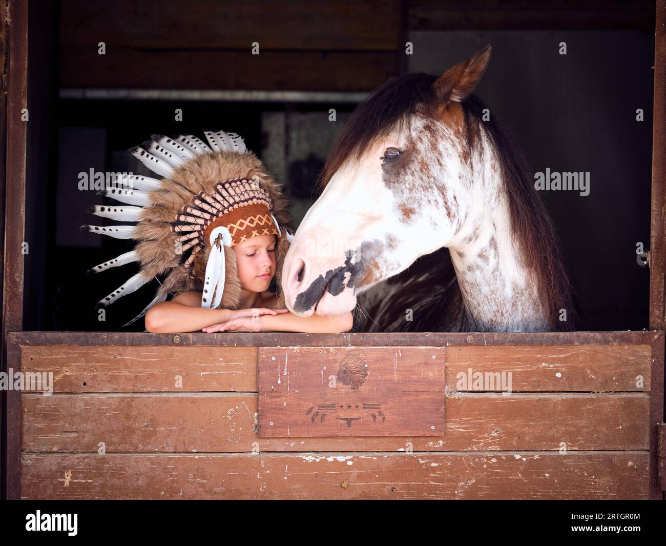 Adorable child in Native American costume leaning on fence of stable ...