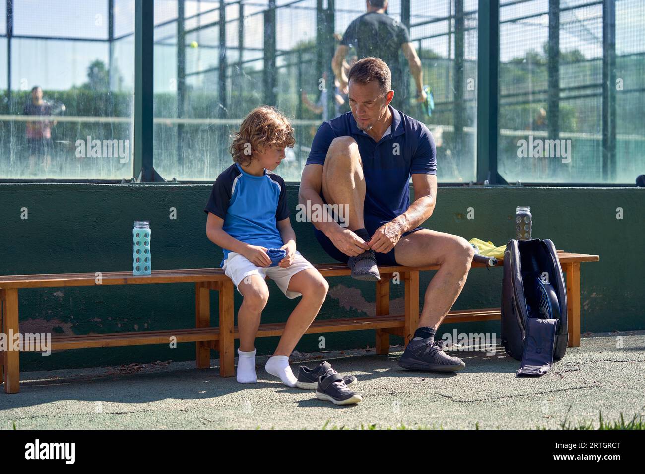 Full body of serious man and boy sitting on bench in street while ...