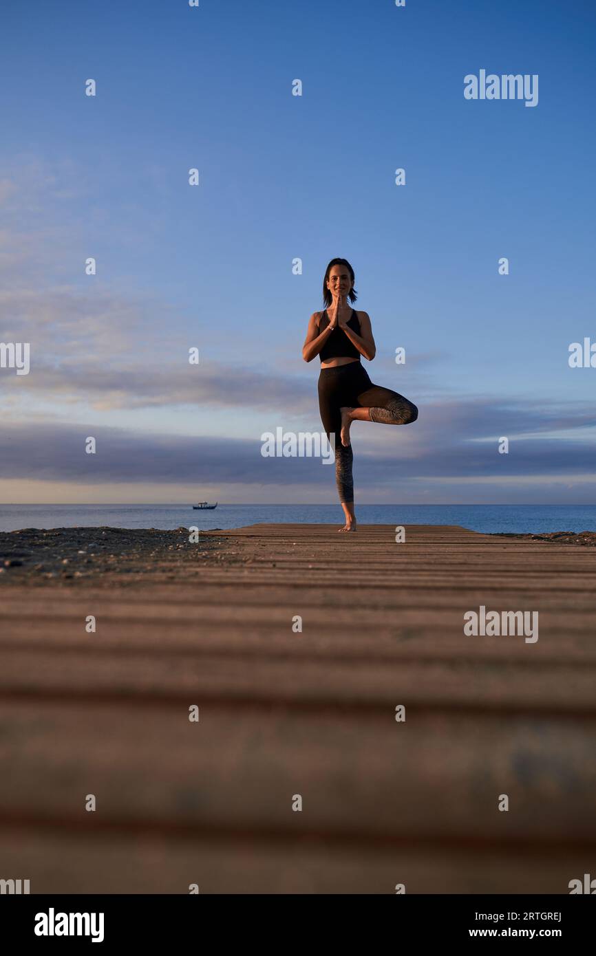 Ground level full body of peaceful female doing Vrikshasana posture ...