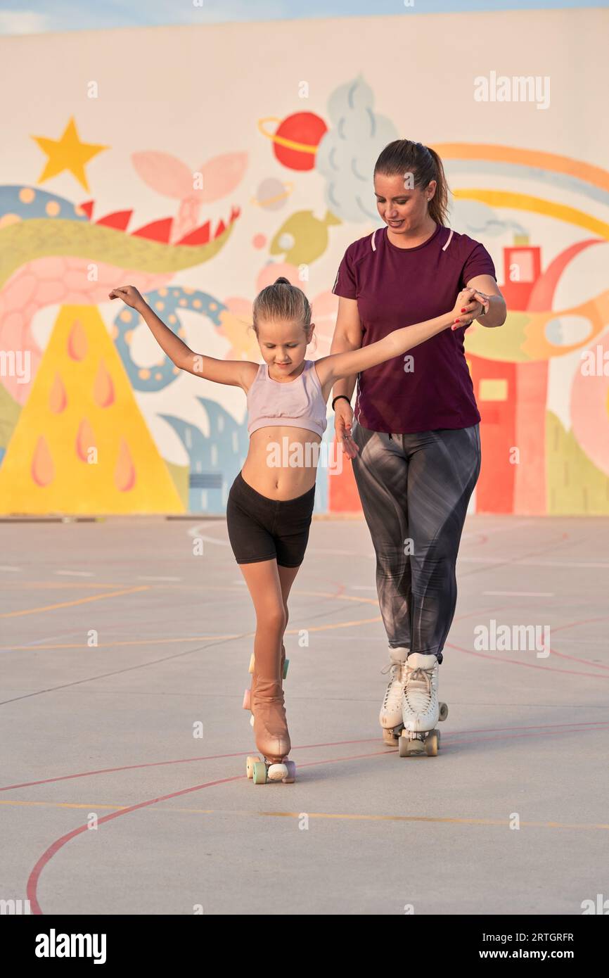 Full body of female coach helping girl to ride roller skates during ...