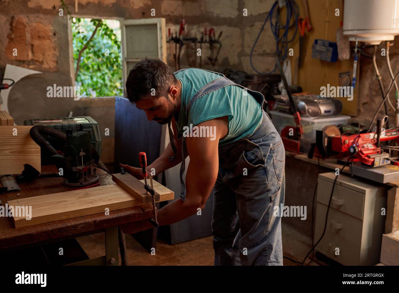 Side view of skilled male carpenter installing clamp on wooden plank ...