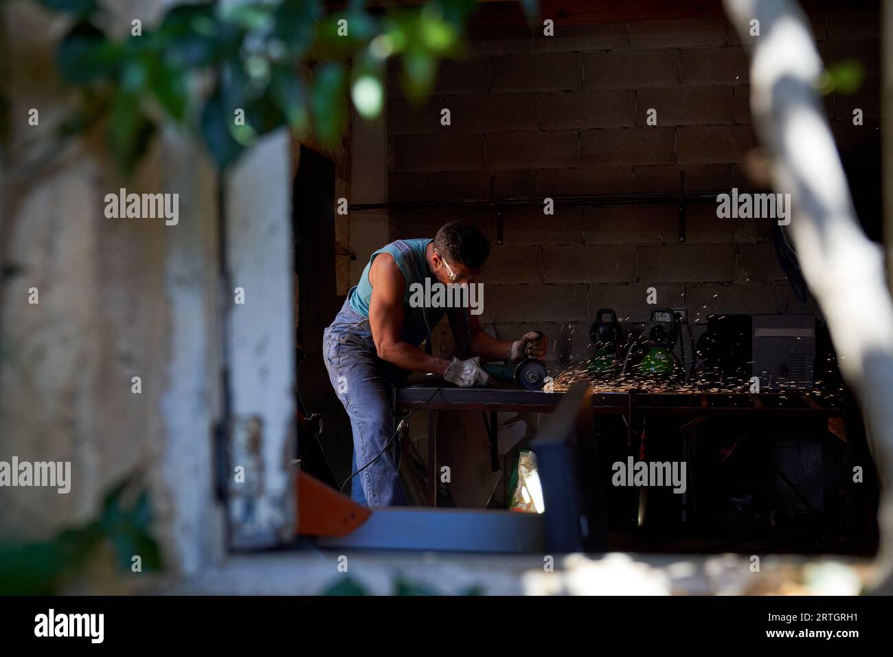 Side view of male carpenter in workwear standing at workbench cutting ...