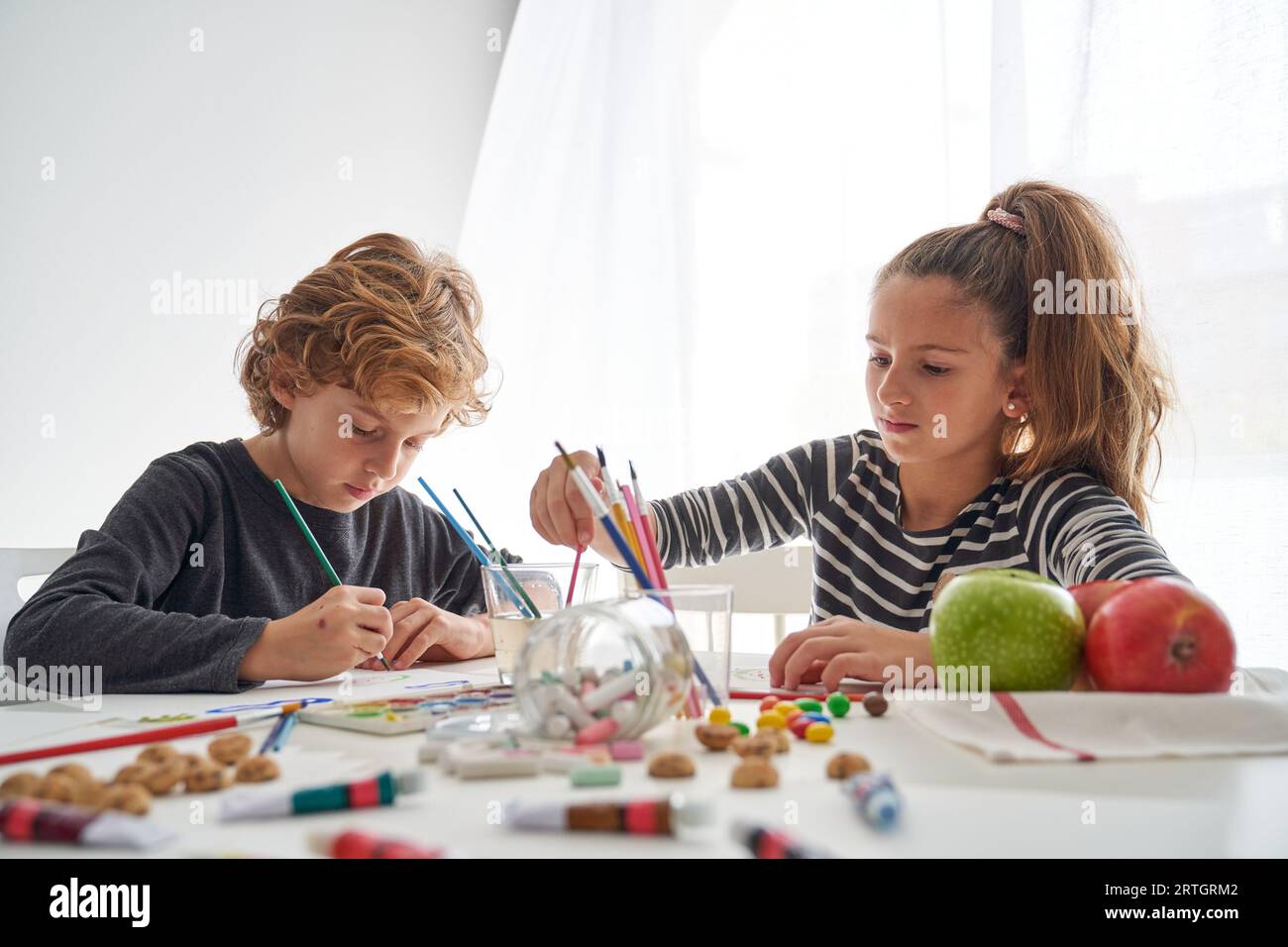 Concentrated children in casual wear painting with paintbrushes while ...
