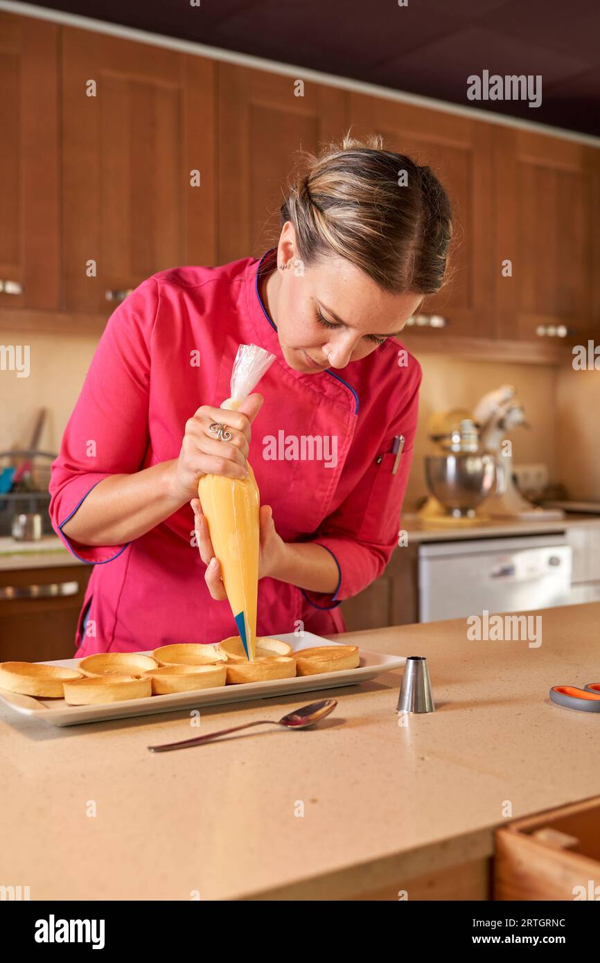 Female pastry chef making peaks of cream on tartlets while standing in ...