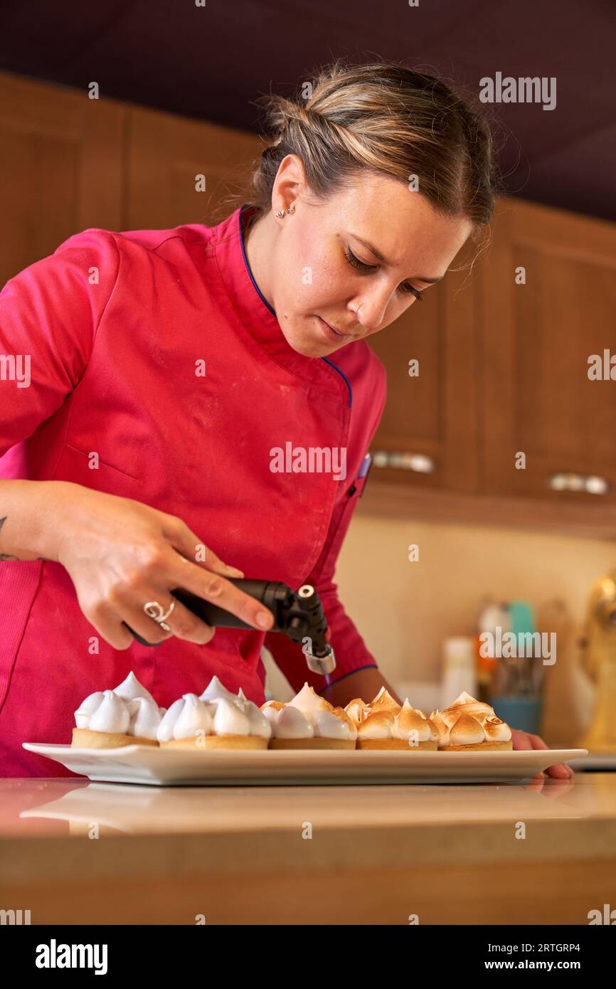 Focused woman burning set of Swiss meringue with gas torch while ...